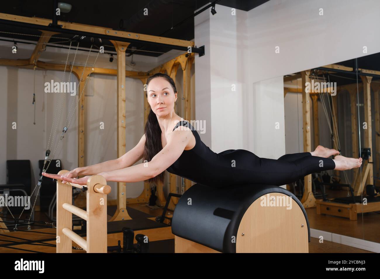 Young girl doing Pilates barre in a gym. Beautiful slim woman in black ...