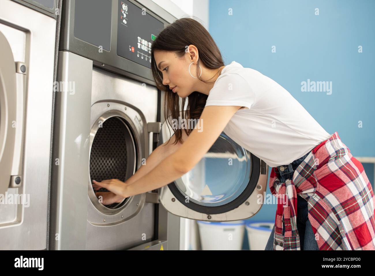 A woman doing laundry at a laundromat while checking her clothes in the dryer Stock Photo - Alamy