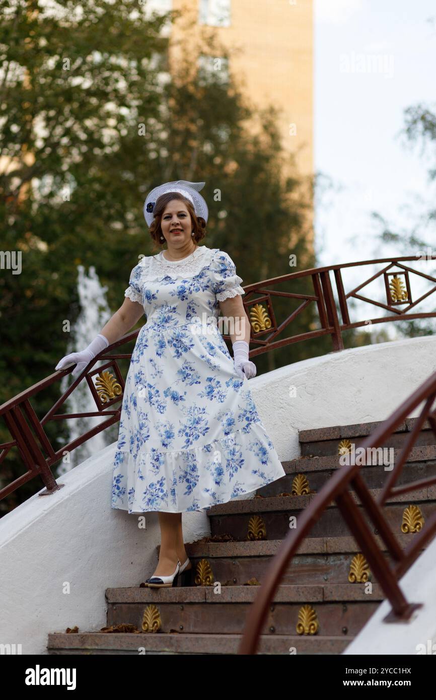 A woman in vintage clothes and a hat stands against the background of a ...