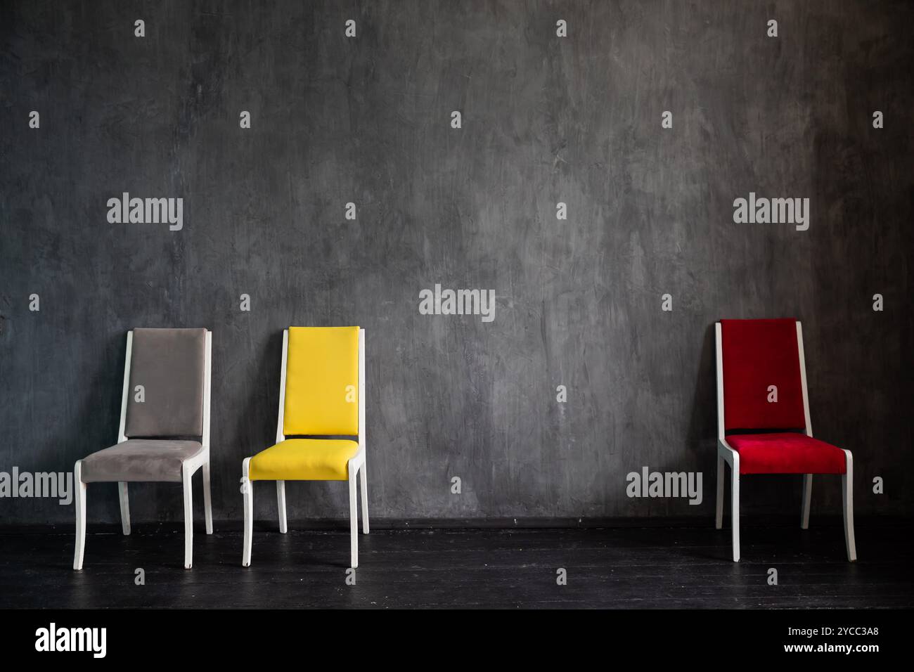 Three chairs of different colors in the interior of an empty gray room ...