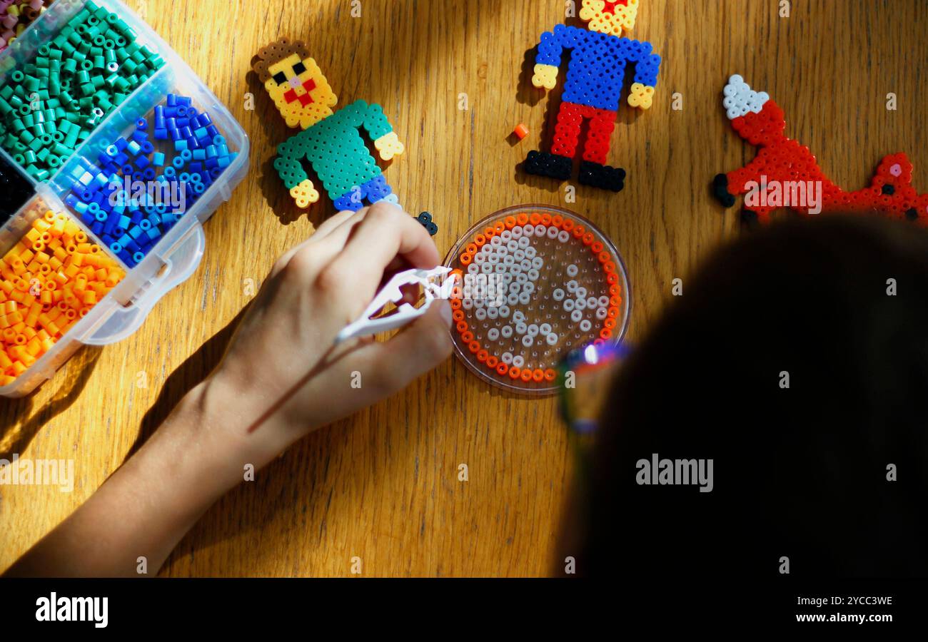 Boy's hand holding tweezers with a bead, creating art toy from fusible ...