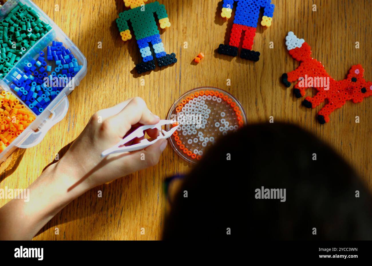 Boy's hand holding tweezers with a bead, creating art toy from fusible ...