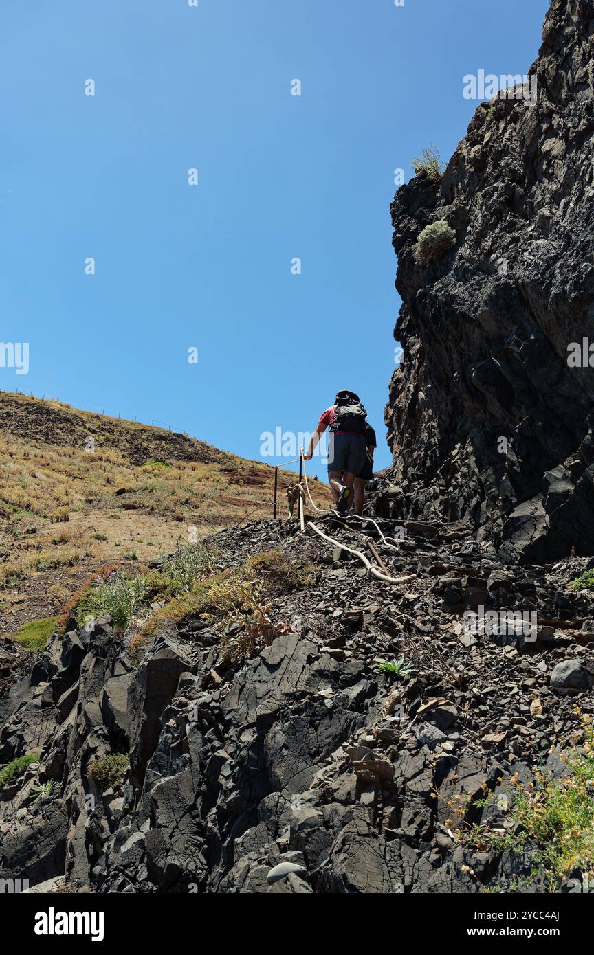A hiker ascending a steep, rocky path along the rugged cliffs of Vereda ...