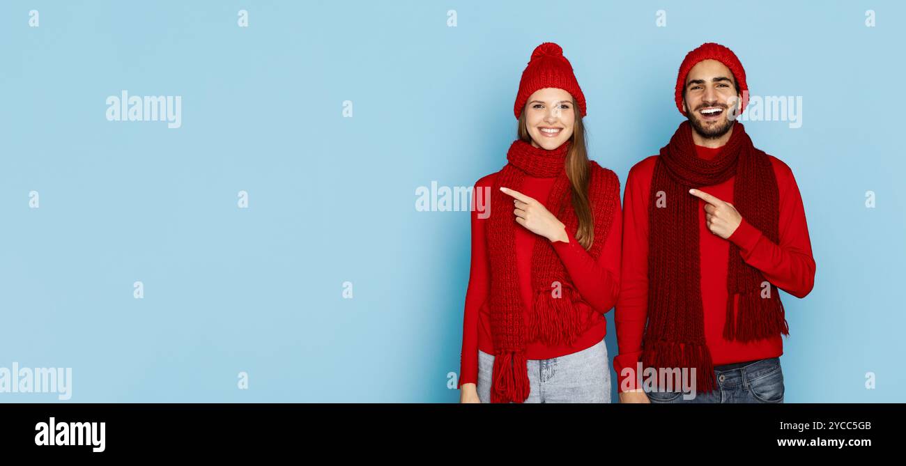 Couple in matching red outfits pointing and smiling against a blue ...