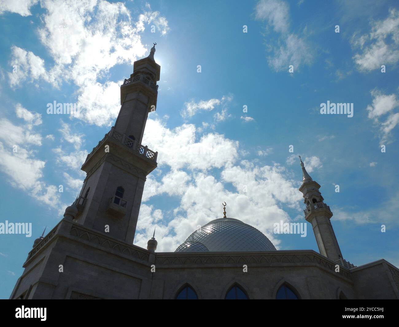 silhouette of mosque against bright blue sky with white clouds, shaded ...