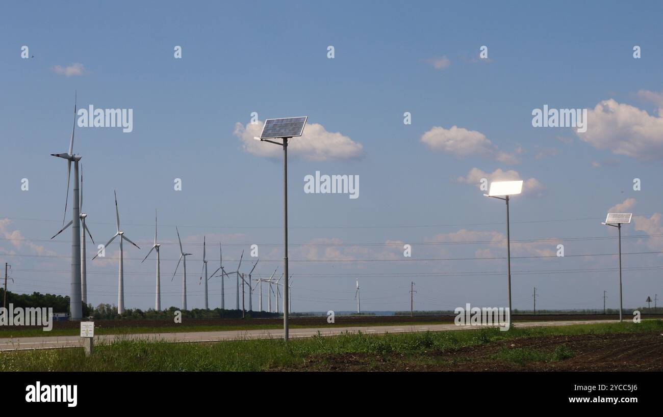 single solar panels on long stands along village road and wind turbines ...