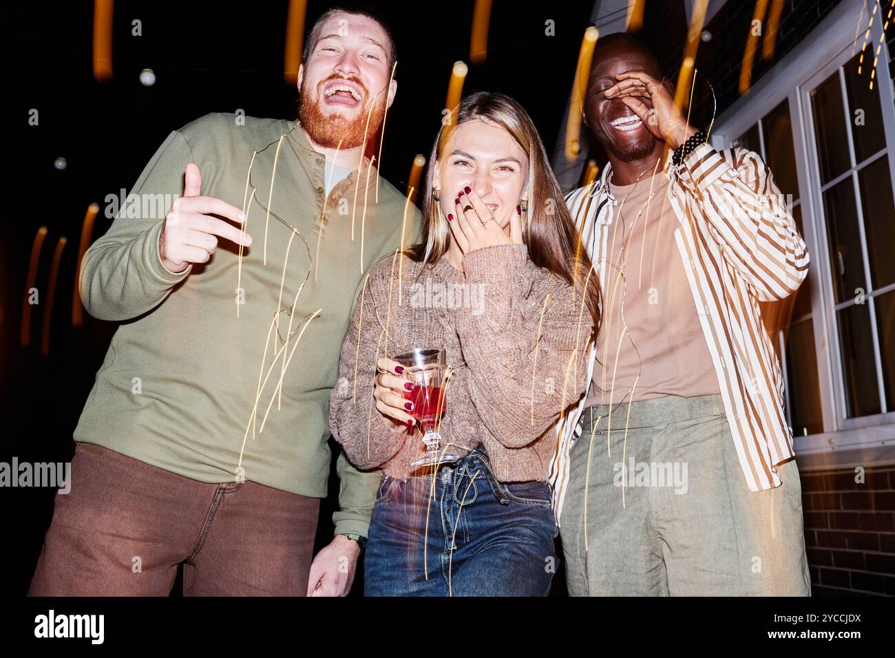 Low angle portrait of three adults partying together outdoors at night ...