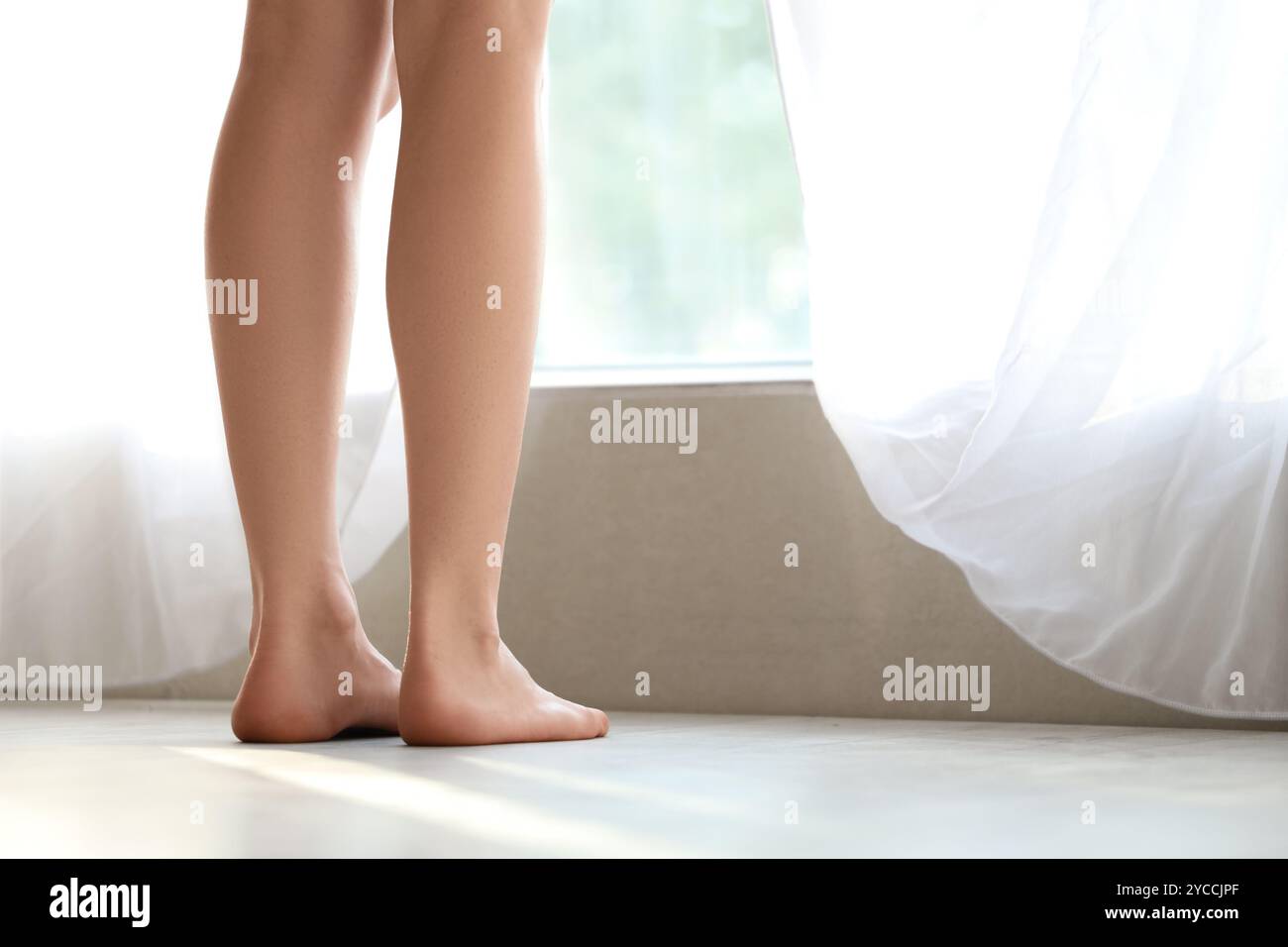 Young woman with flat feet on floor near window at home, back view ...