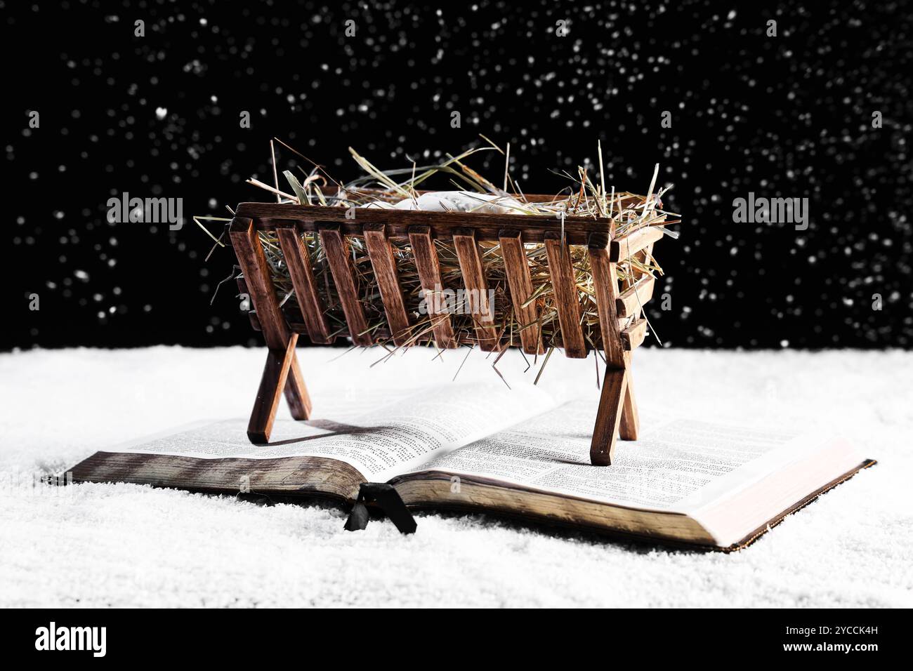 Manger with baby Jesus, hay and Holy Bible on snow against dark ...