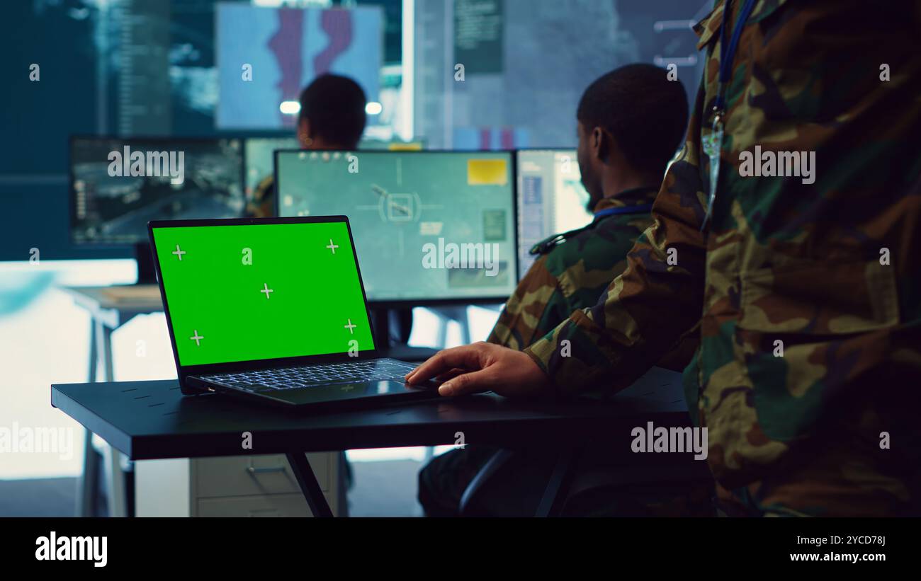 Army officer studies isolated greenscreen display on a laptop in ...