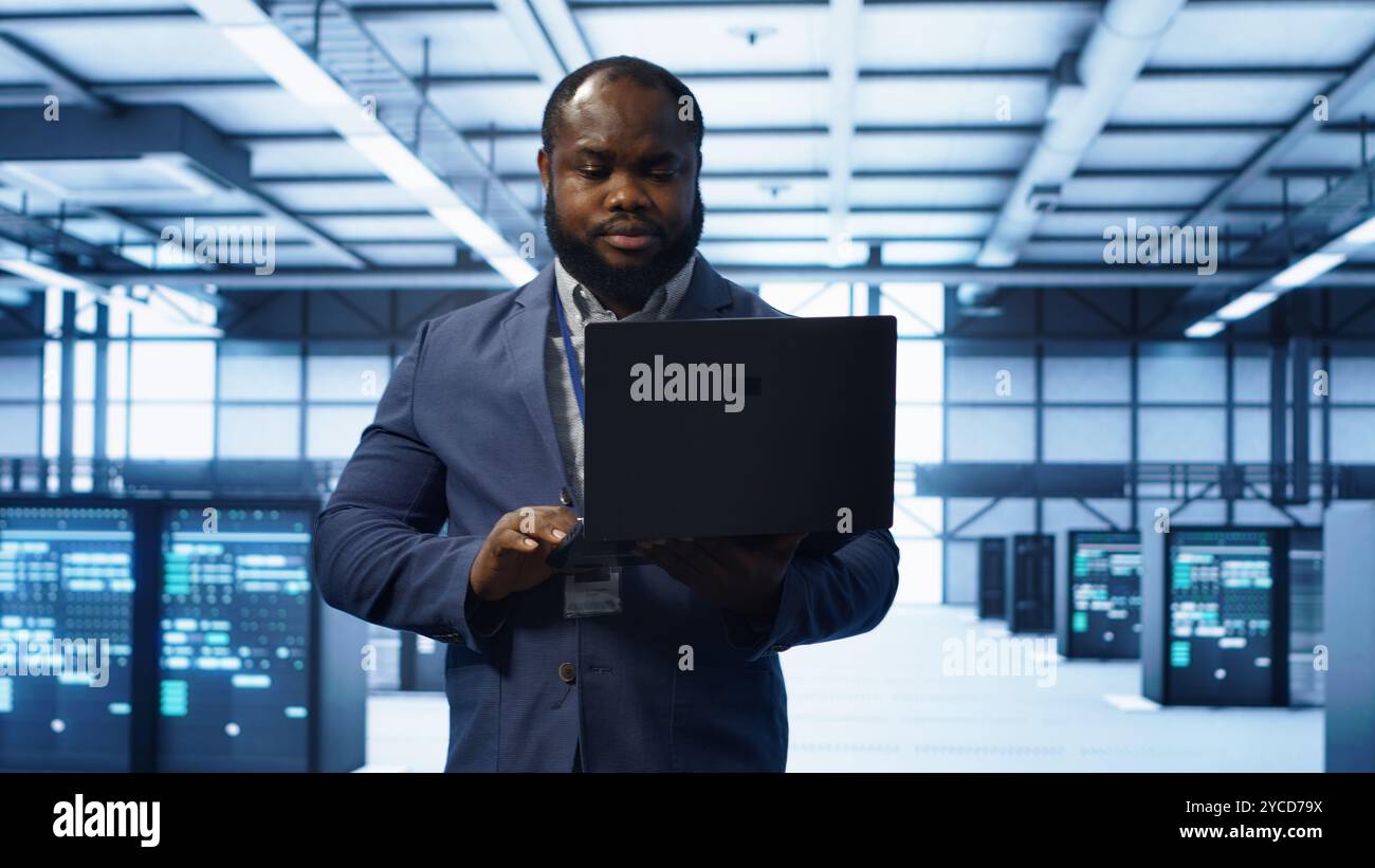 IT engineer working on laptop in modern data center, overseeing server operations, system ...