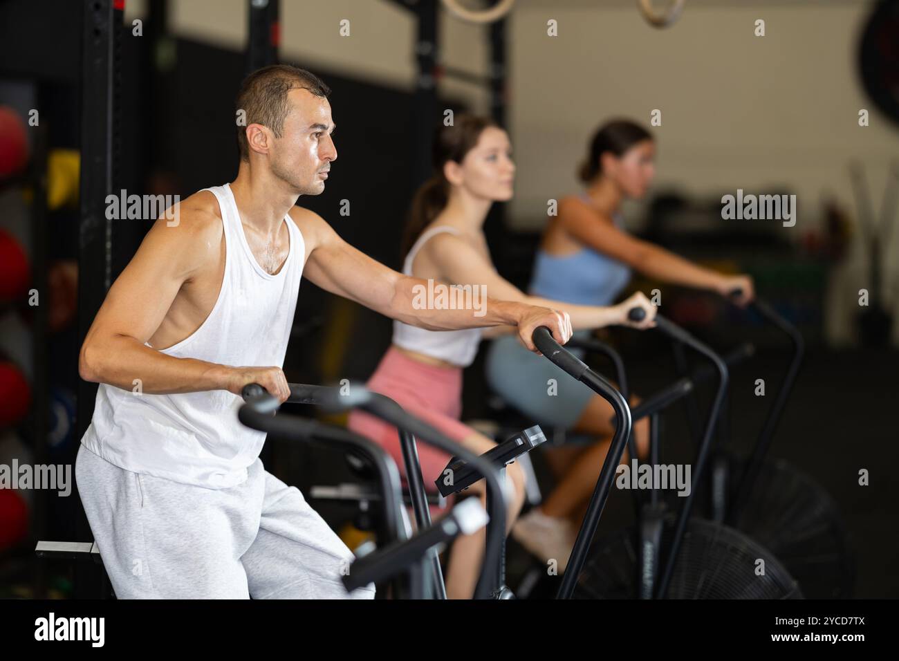 Man doing air-bike with group of sporty people exercises in well ...