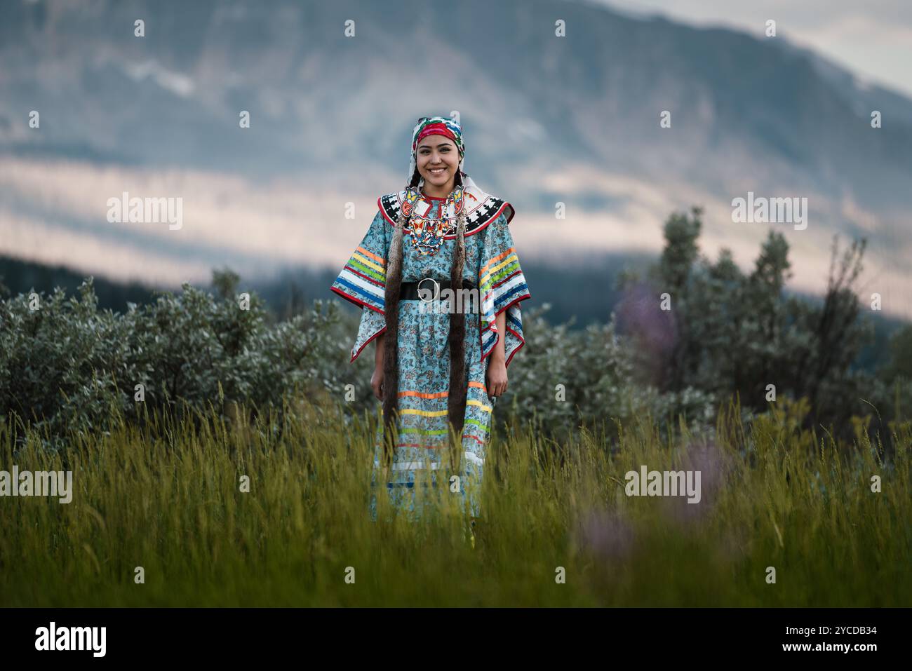 Indigenous woman in traditional attire standing in a lush green field ...