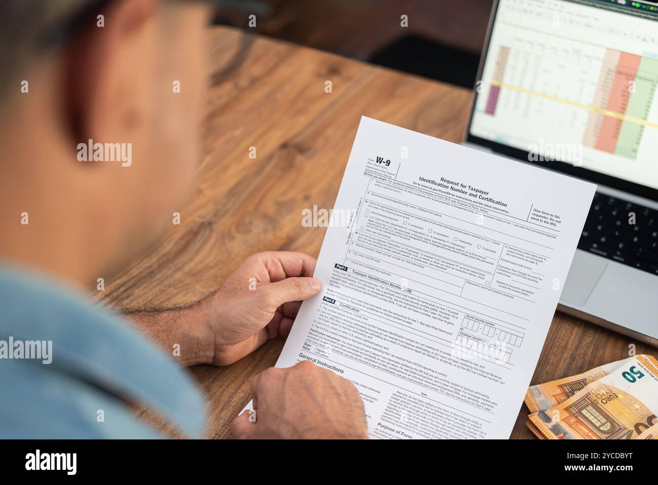 Real estate agent carefully checks W-9 form on table with laptop and ...