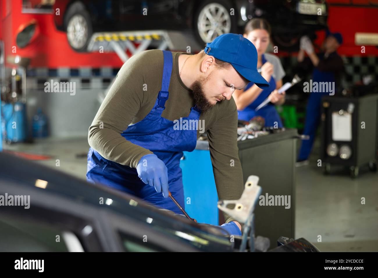 Professional mechanic man in uniform repairing car in auto repair ...