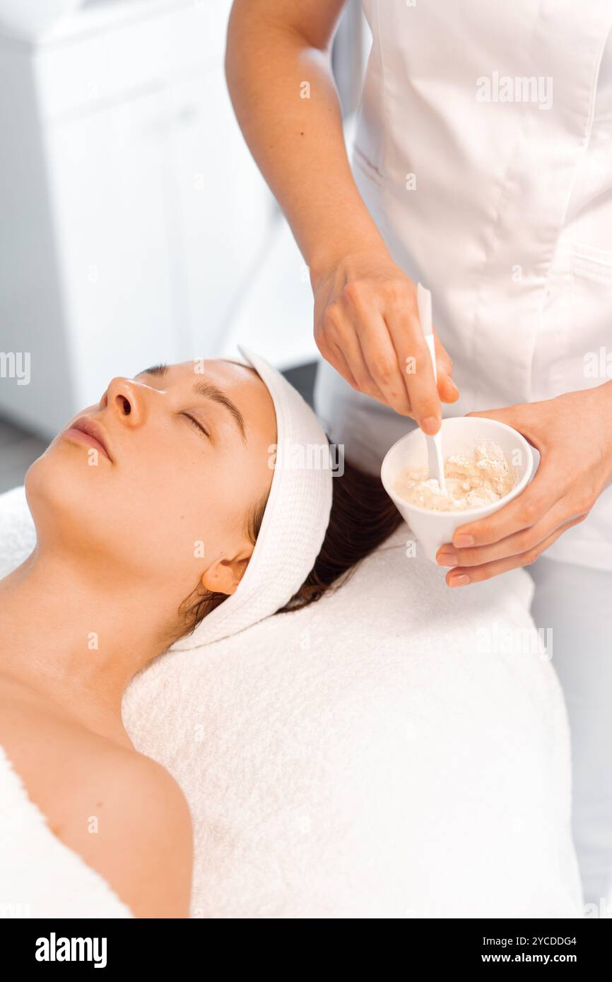 Dermatologist preparing face pack for female client lying on massage ...