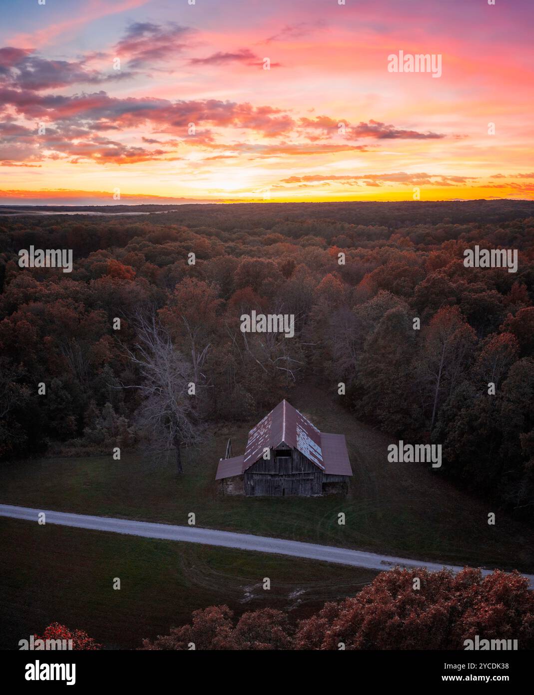 An old barn with a metal roof and weathered siding sits in a clearing ...