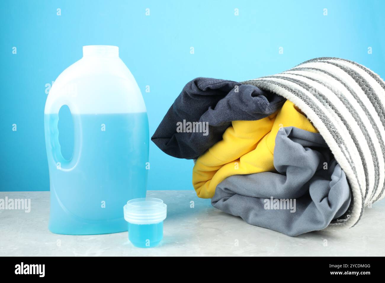 Laundry detergent in bottle, cap and clothes on grey marble table ...