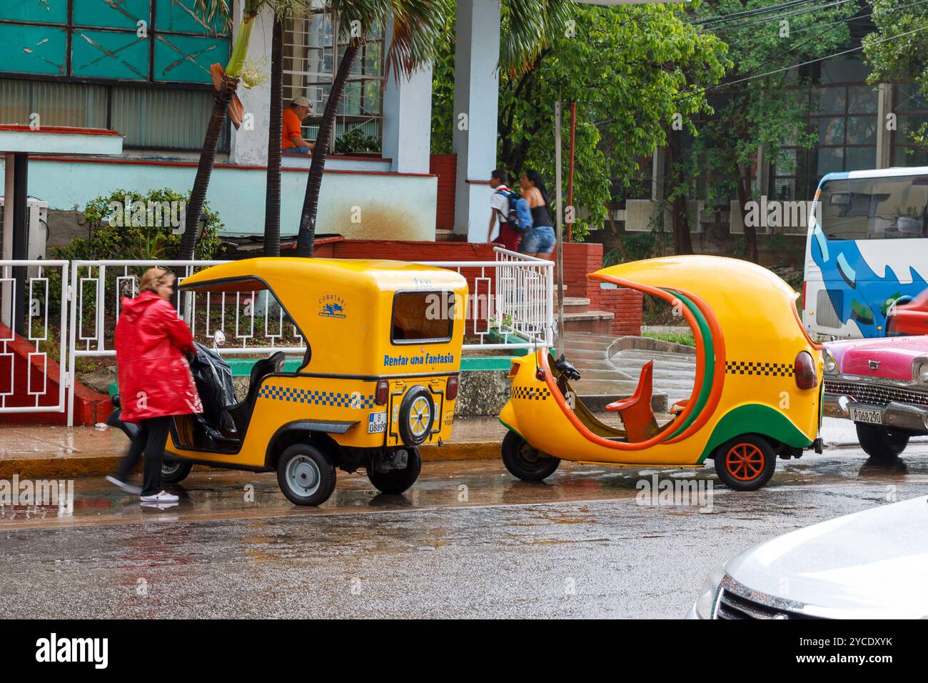 Tourist in a red wet coat entering a typical yelllow three wheel coco ...
