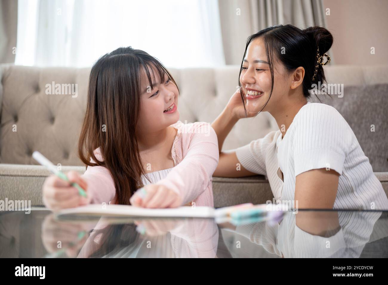 A caring and kind Asian mom is teaching her daughter to draw, enjoying quality family time ...
