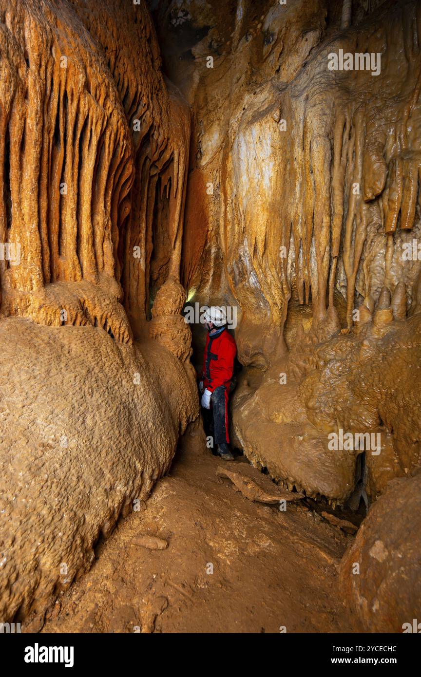 A speleologist with helmet and headlamp exploring a cave with rich ...