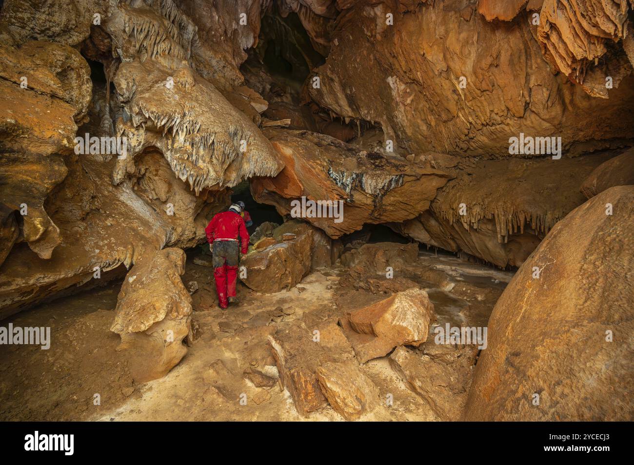 A speleologist with helmet and headlamp exploring a cave with rich ...