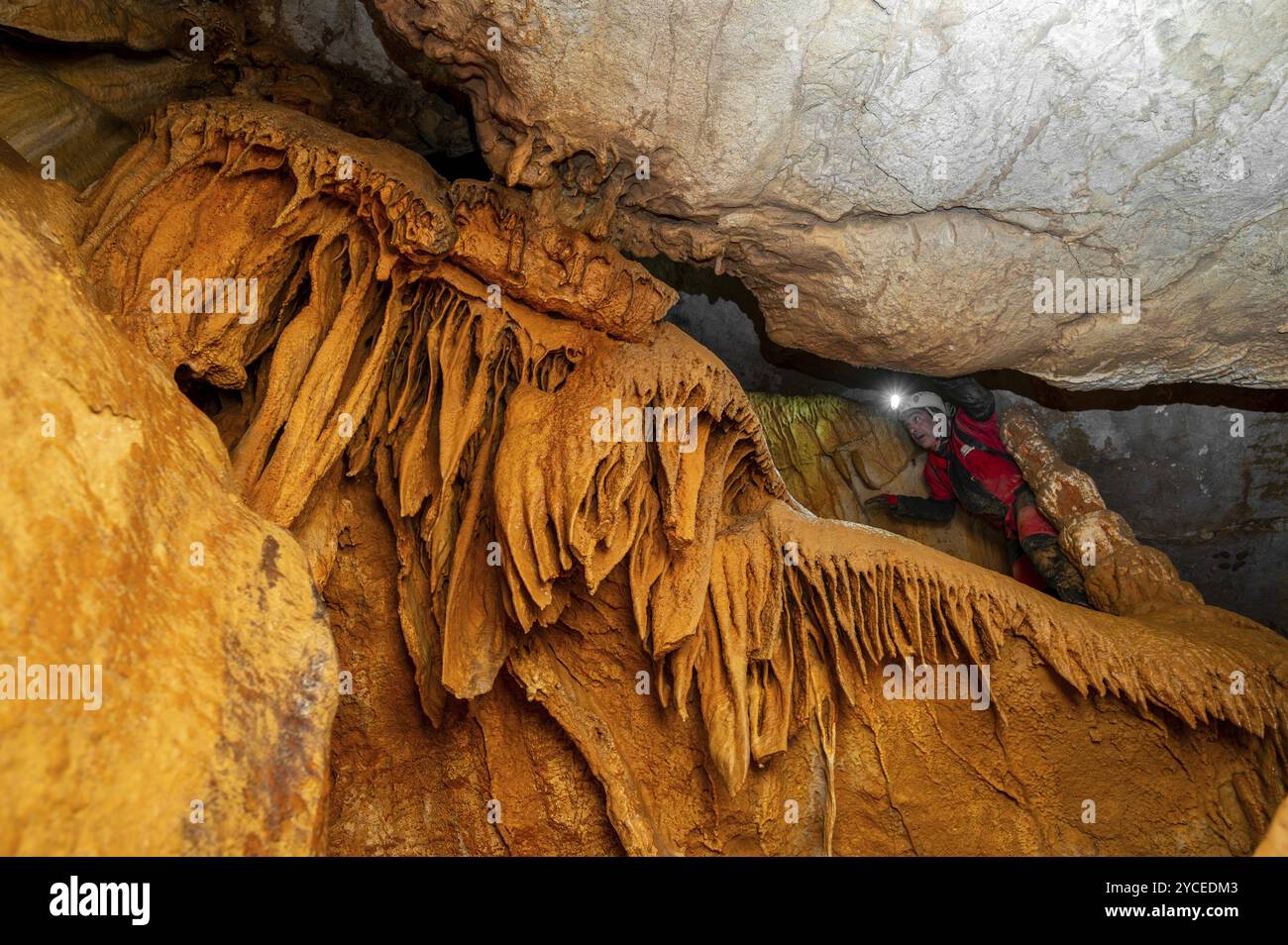 A speleologist with helmet and headlamp exploring a cave with rich ...