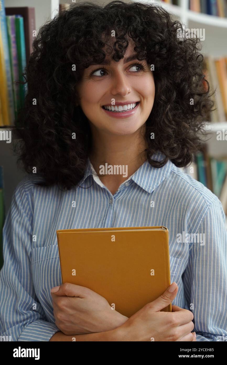 Sweet curly-haired young girl at the bookshelves in the library Stock ...