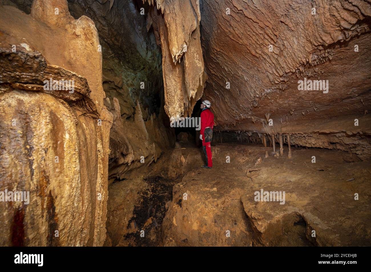 A speleologist with helmet and headlamp exploring a cave with rich ...