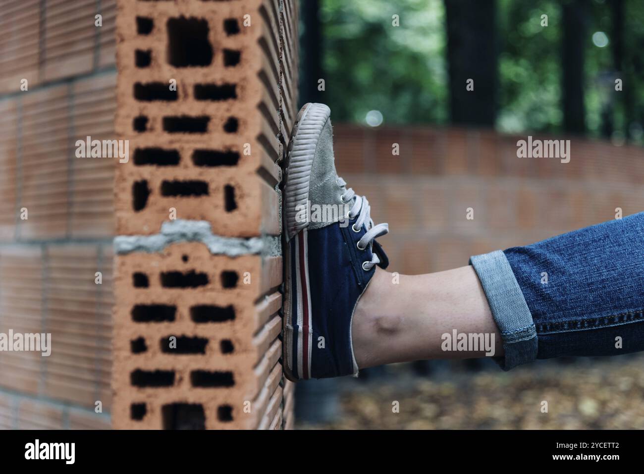 Woman wearing sneakers leaning his foot on curved brick wall in city ...