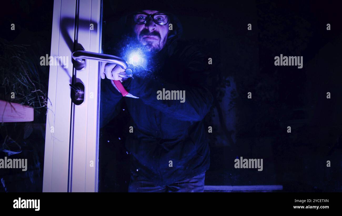 Burglar enters the house, breaking through the glass door with ...