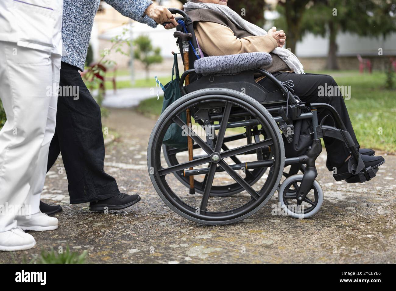 Senior woman in wheel chair with relative and nurse caregiver, outdoors ...