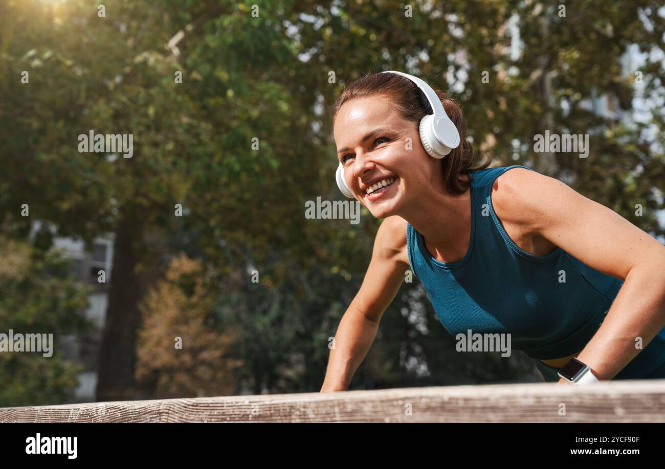 Fitness woman in headphones doing exercises in city park, she does push ...