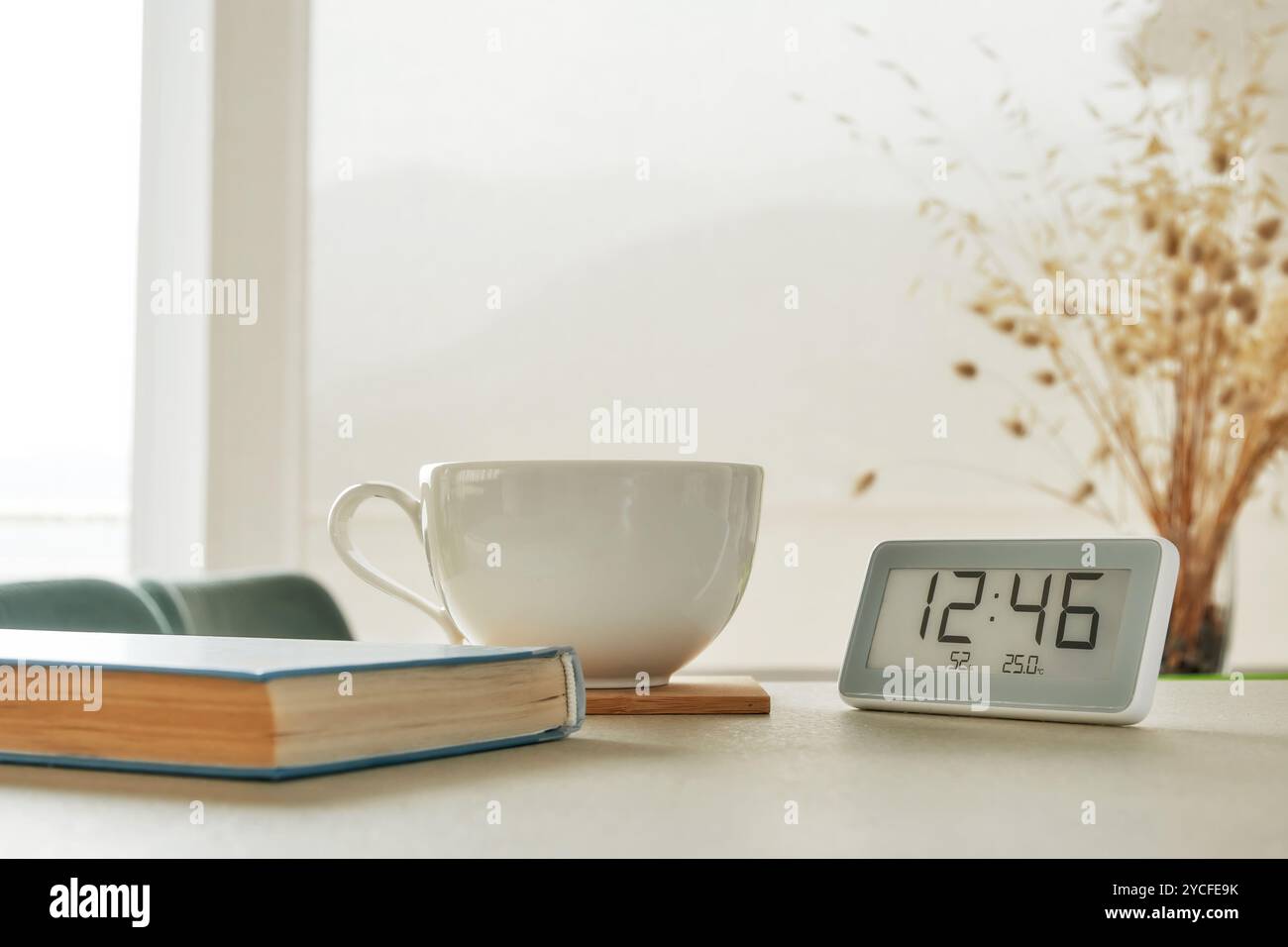 A digital clock with white background shows the time 12:46, a white cup ...
