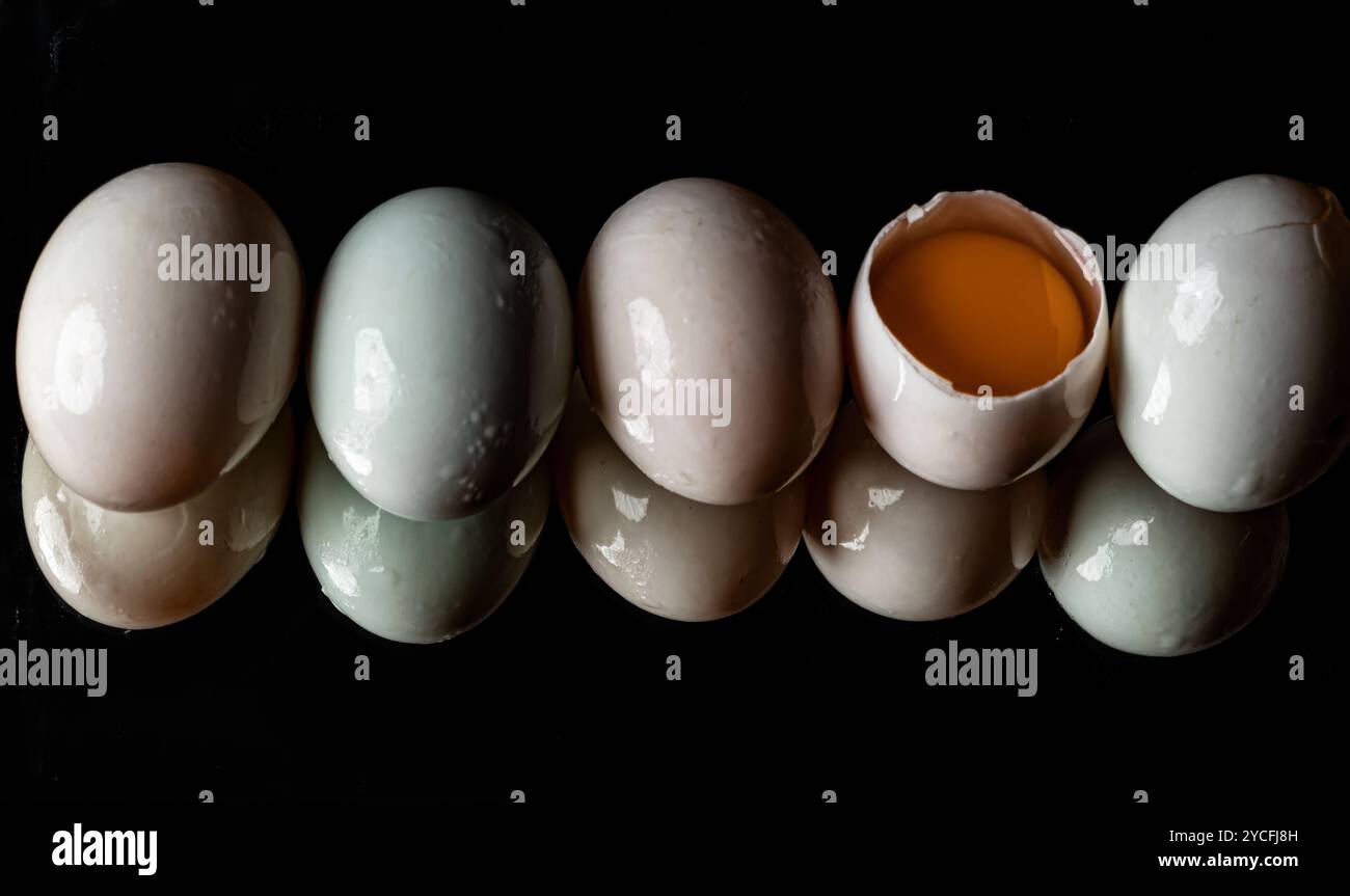 Five raw duck eggs are sitting in a row with an egg broken in half ...