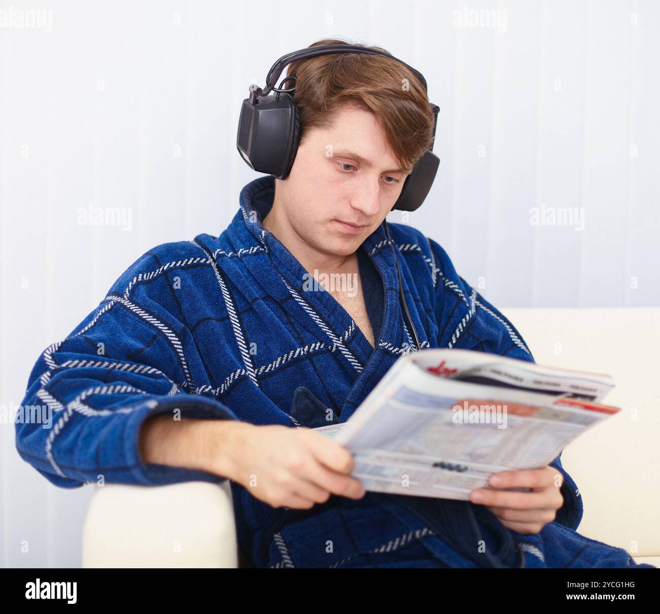 Man in big ear-phones on sofa reads newspaper Stock Photo - Alamy