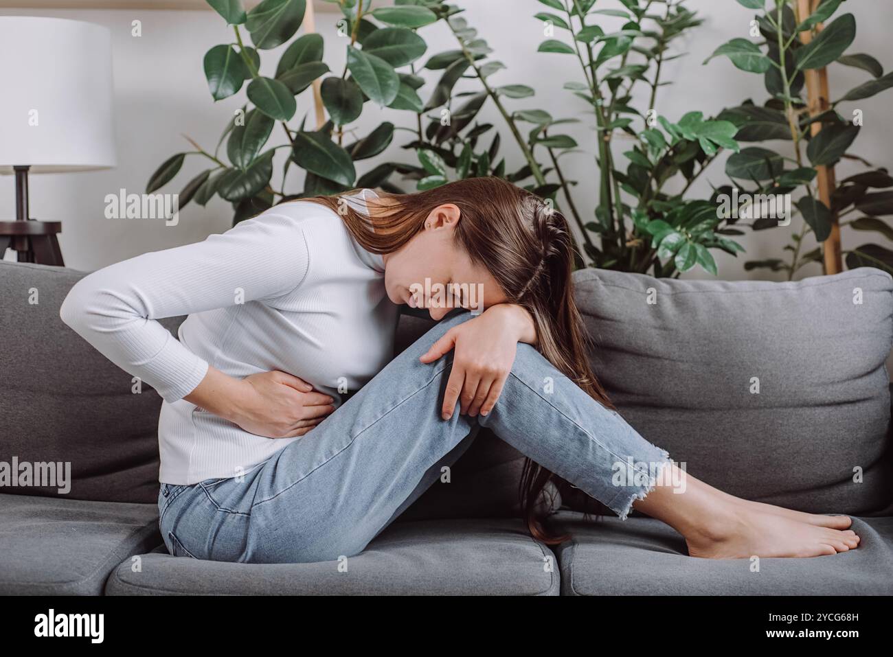 Upset female sitting on sofa suffering from indigestion flatulence ...