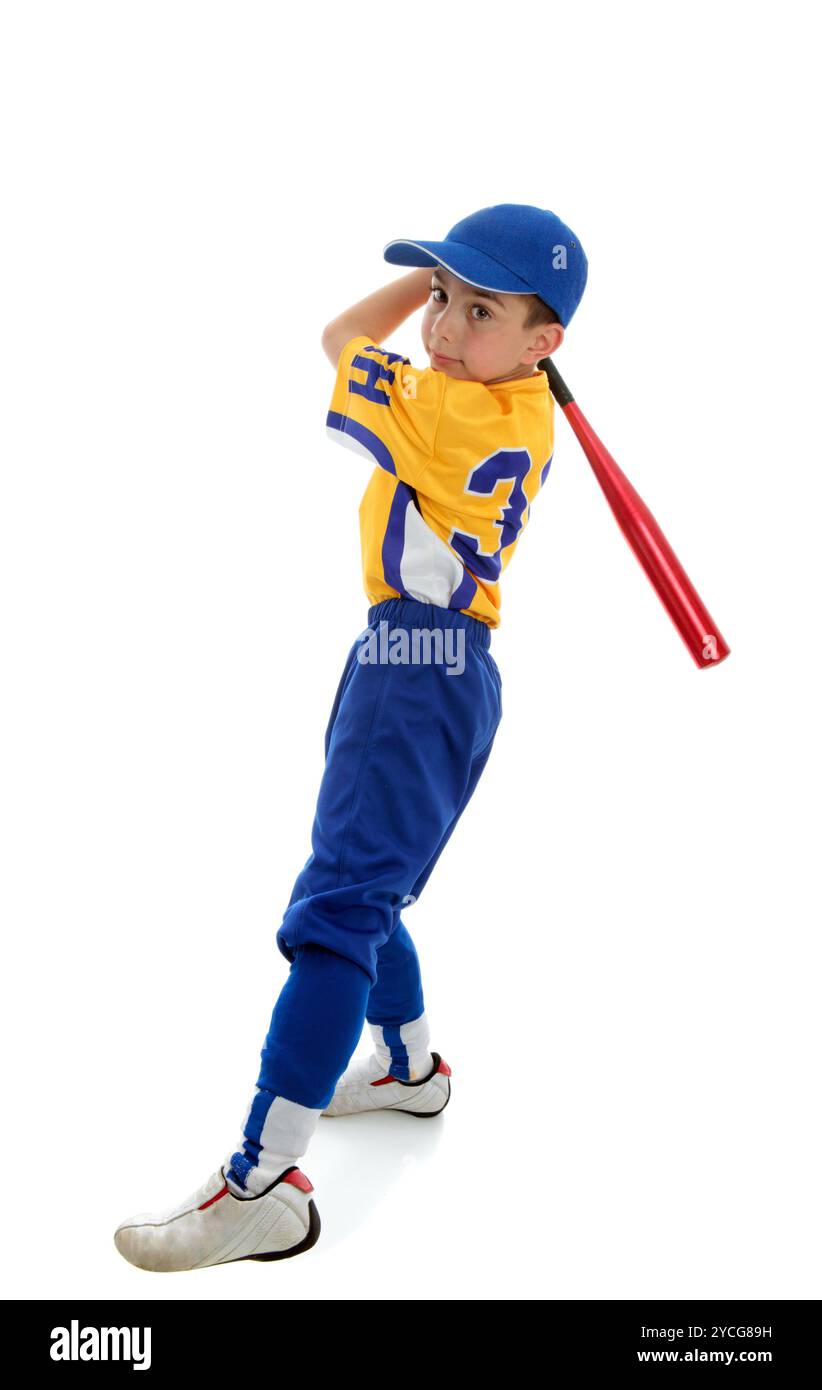 A young boy in a softball, baseball or t-ball uniform swings a bat ...