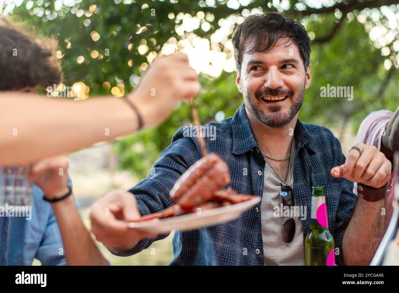 Portrait of cheerful man sharing food during outdoor gathering. Natural ...