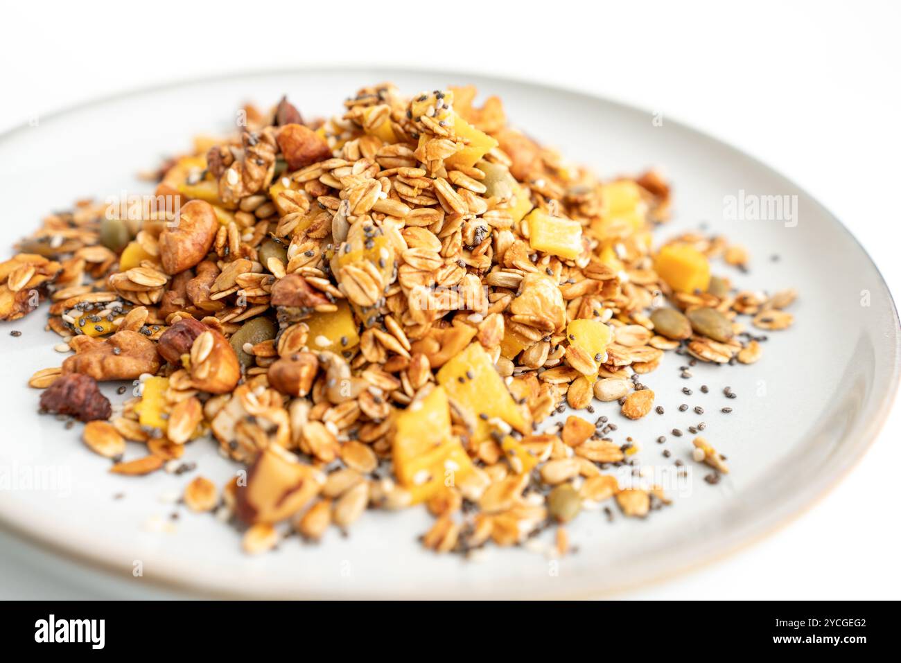 A bowl of granola with nuts and seeds on a white plate. The granola is ...