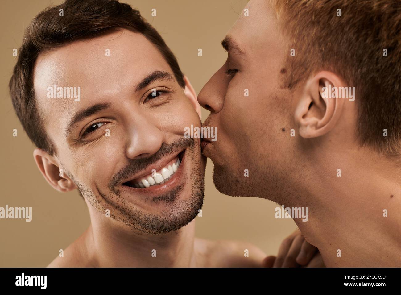 Two young men embrace joyfully while sharing a tender kiss, radiating ...