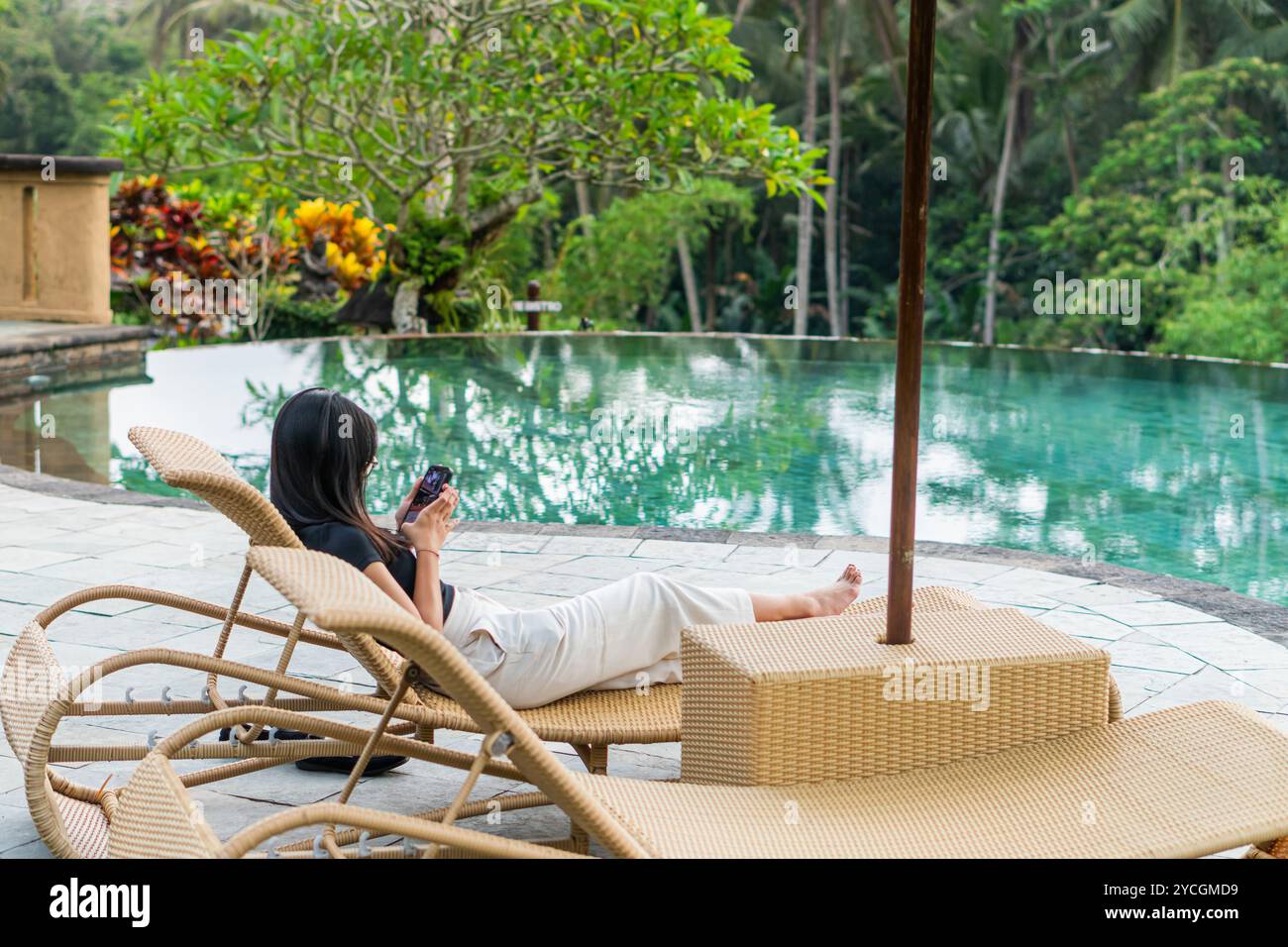 A woman lounging by an infinity pool in a tropical setting, using her ...