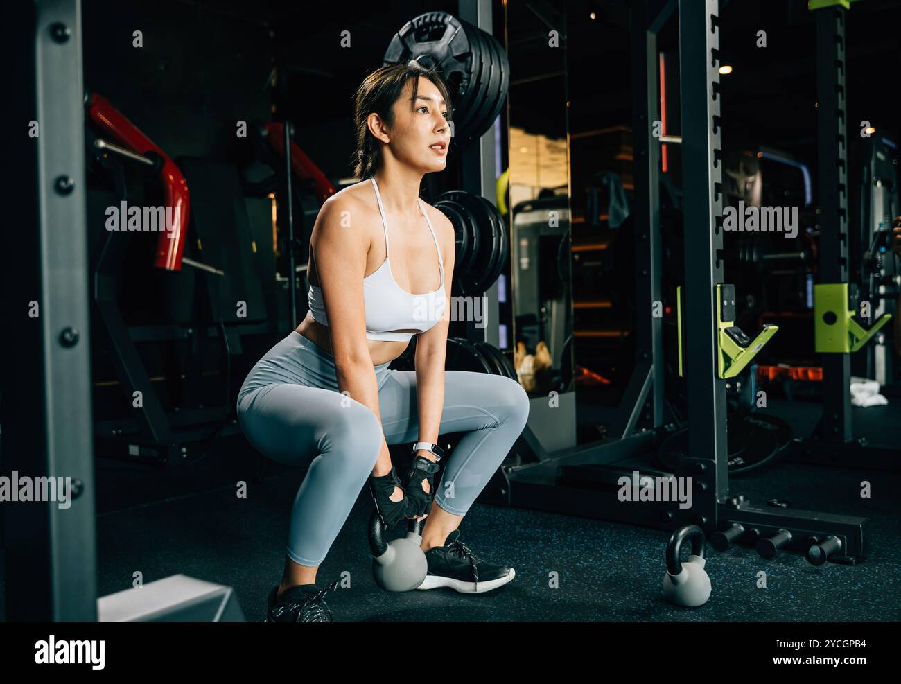 Asian woman holding and lifting a weight kettlebell in fitness gym ...