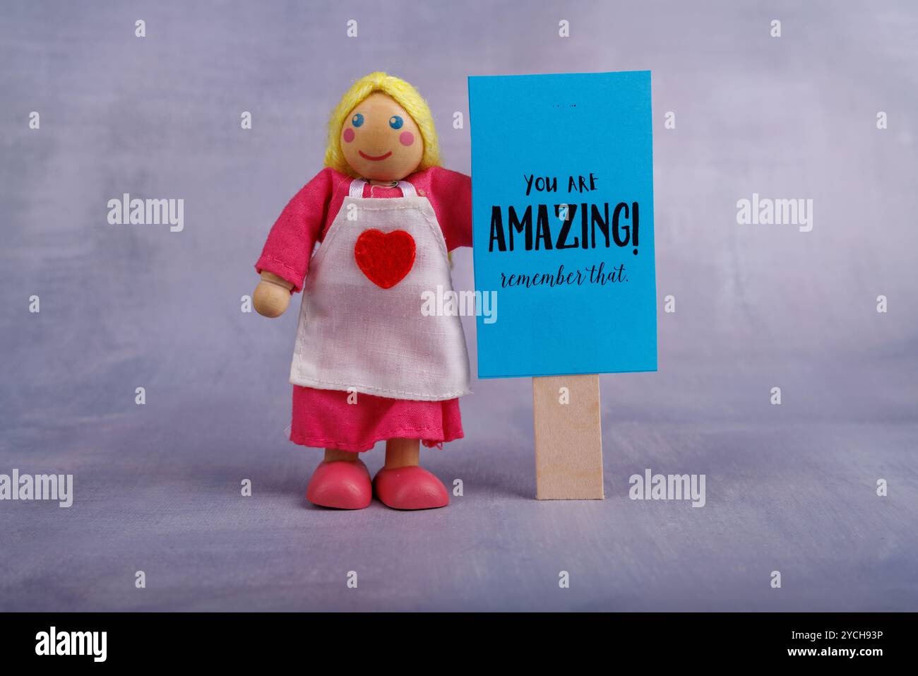 This wooden doll holds a blue sign featuring an uplifting message of ...