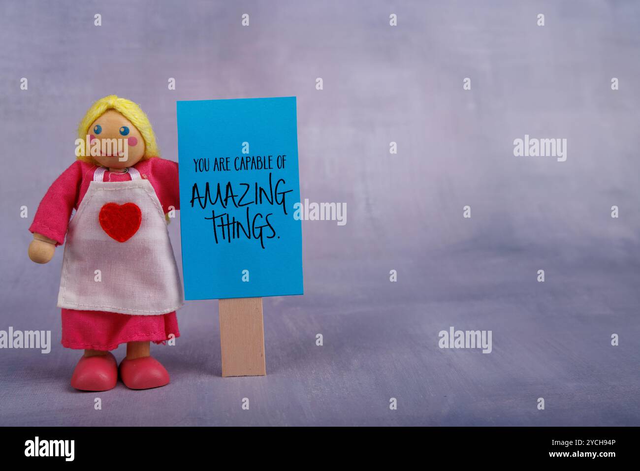 A wooden doll holds a blue banner with a phrase of encouragement ...