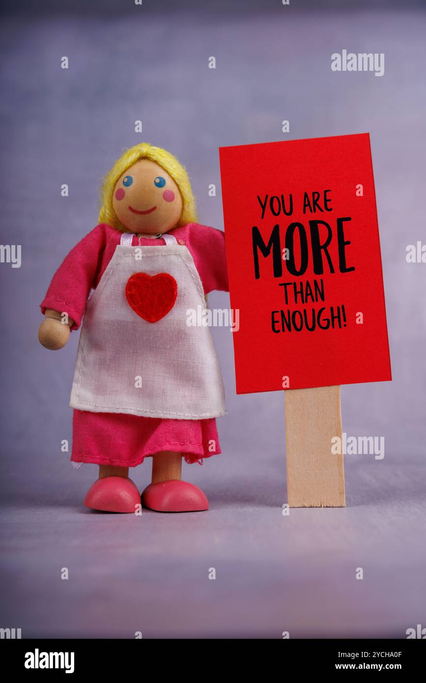 A wooden doll presents a red sign with a positive quote, inspiring ...