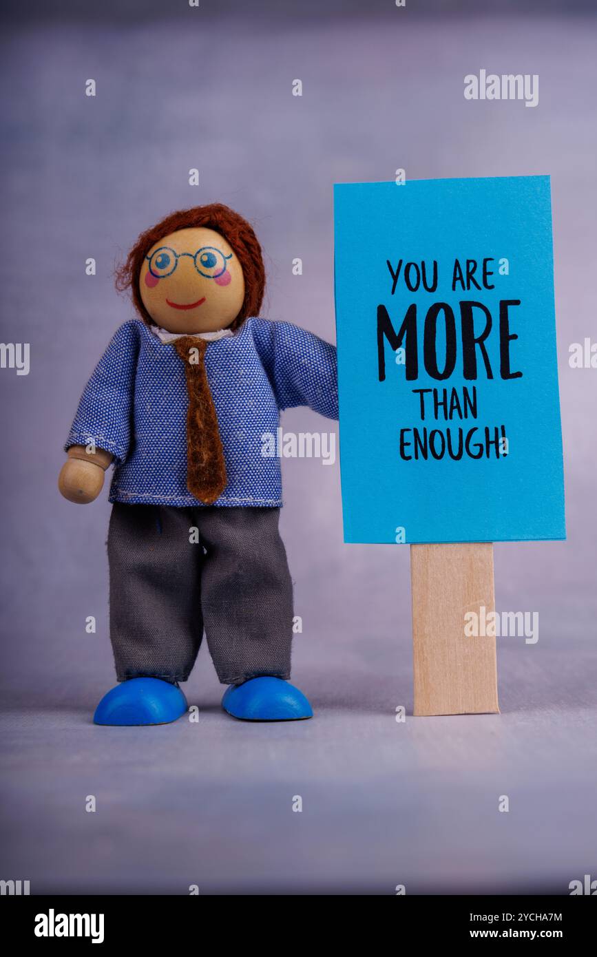 A wooden toy man holds a blue sign with a motivational message. The ...