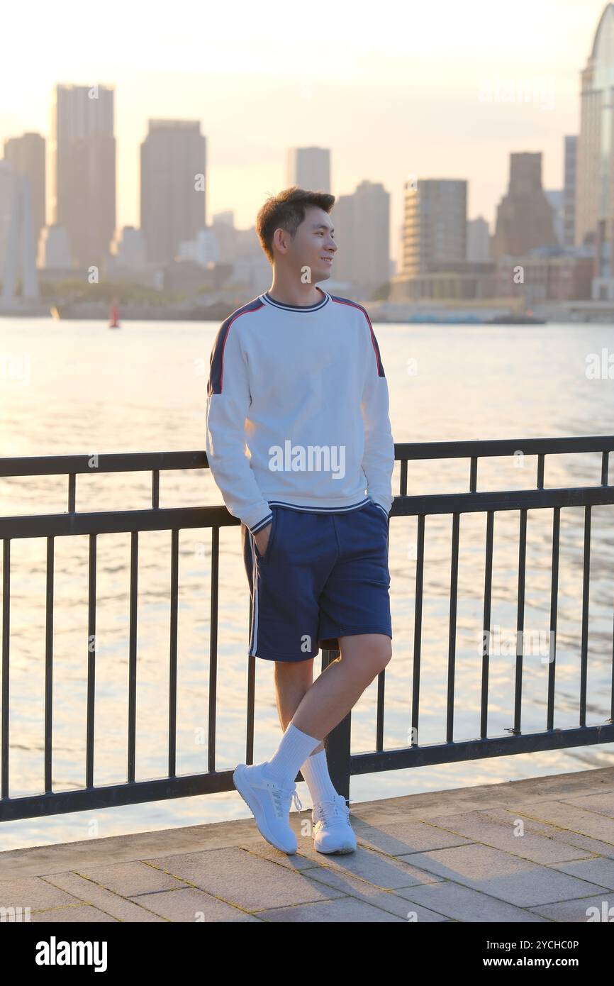 smiling handsome Asian young man standing at dusk outdoor, full length ...