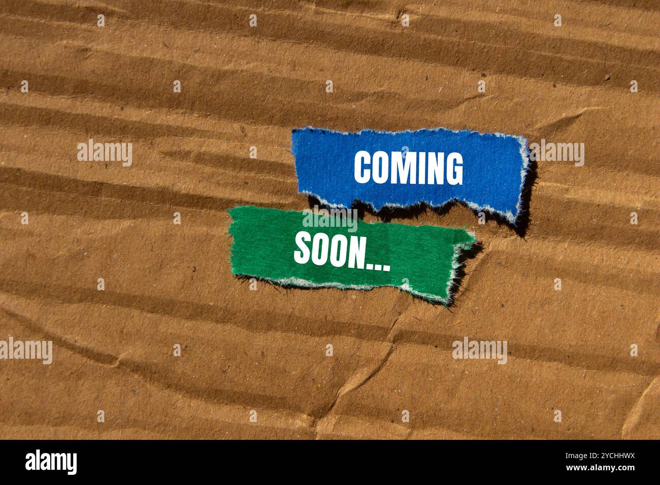 Coming soon message written on ripped torn paper pieces with cardboard ...