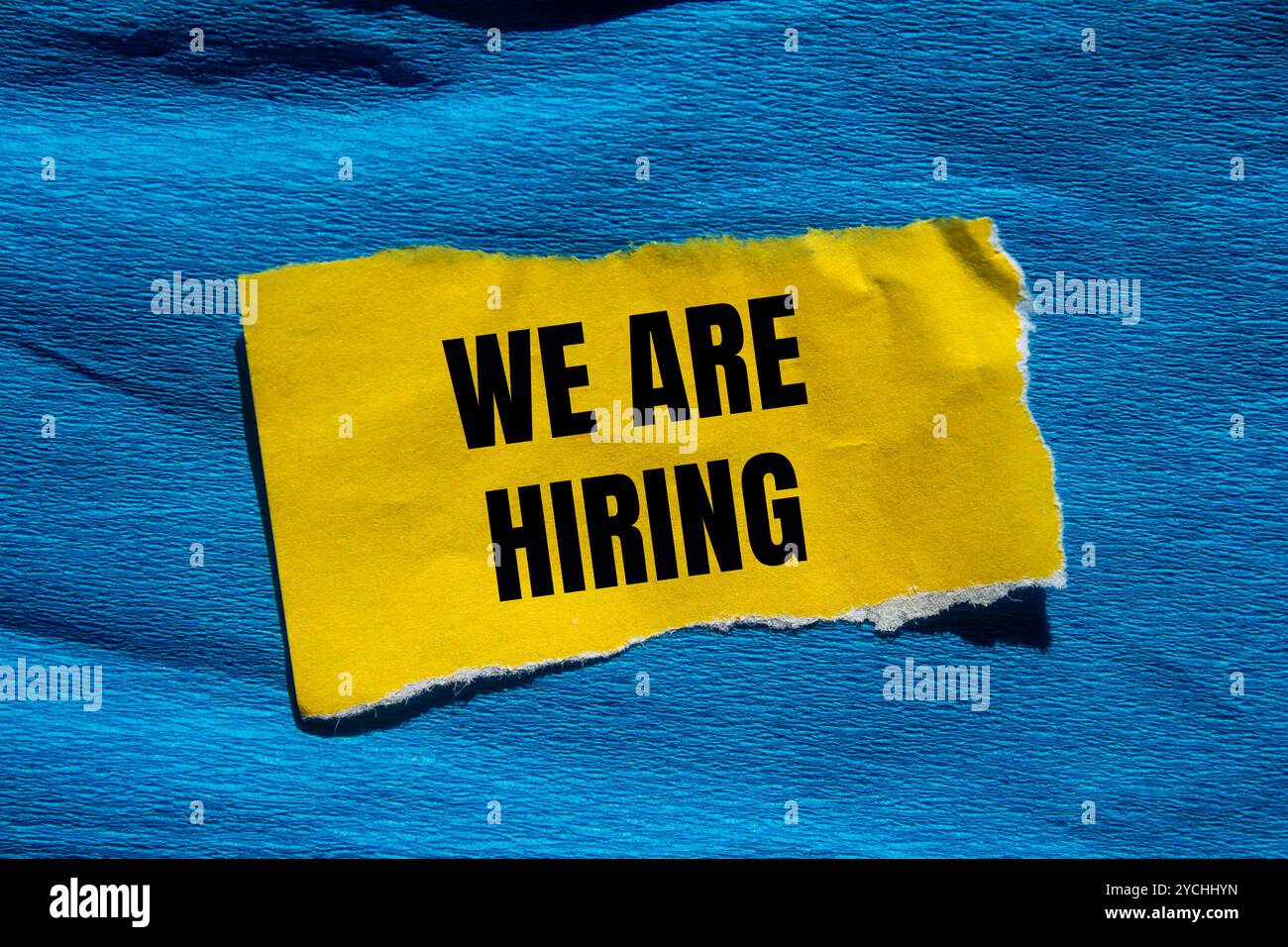 We are hiring message written on ripped torn yellow paper piece with blue background. Conceptual ...